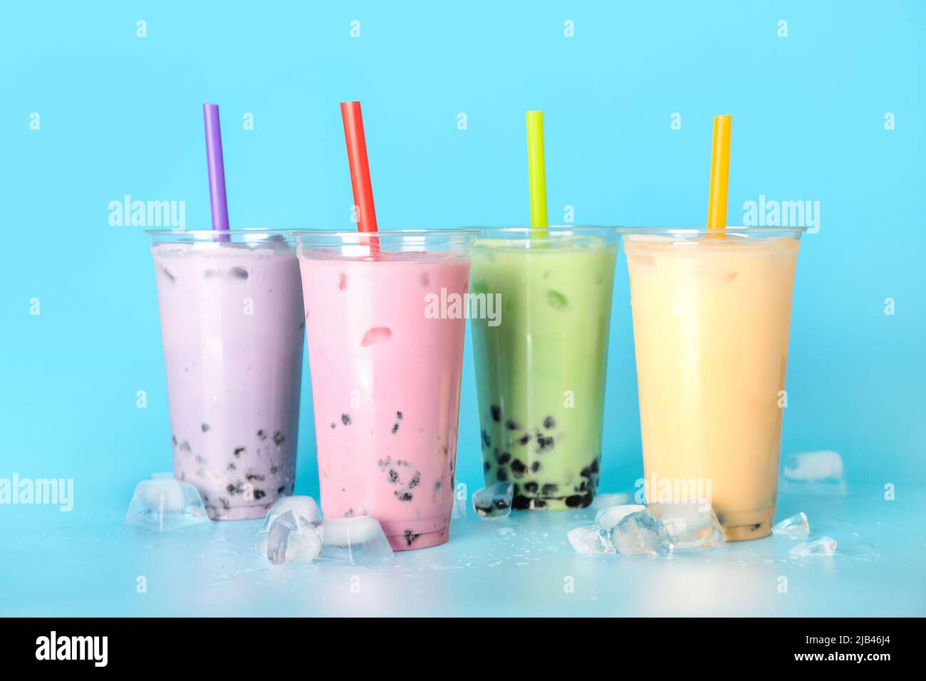 Plastic cups of different tasty bubble tea and ice cubes on blue ...