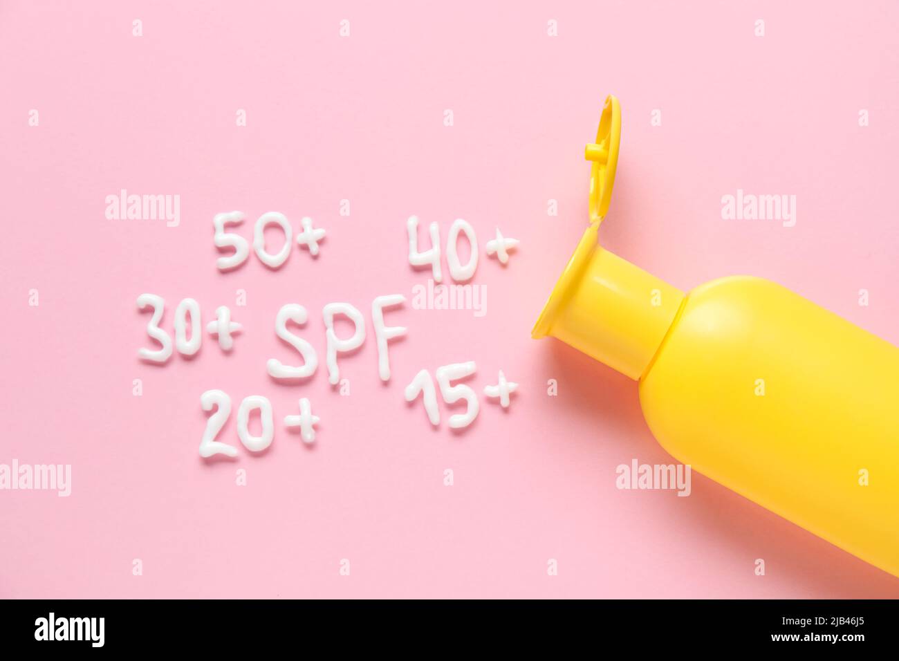 Word SPF and numbers made of cream with bottle of sunscreen on pink ...