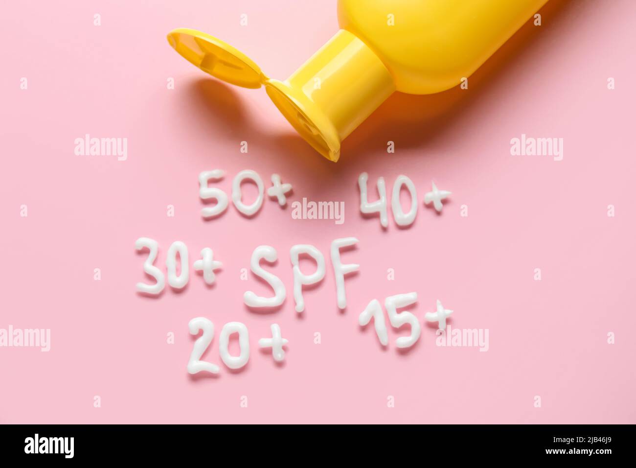 Word SPF and numbers made of cream with bottle of sunscreen on pink ...