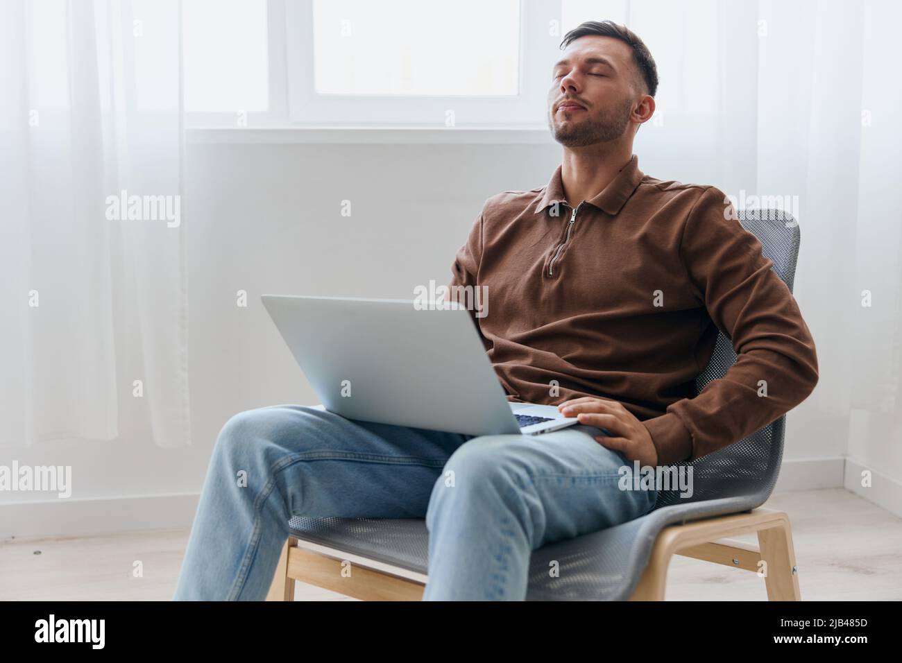 Sleepy tired unhappy tanned young man sitting with laptop at home try ...
