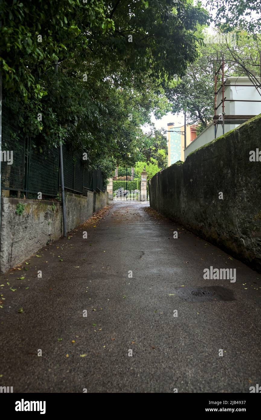 Side road bordered by concrete walls and trees with a gate at the end ...