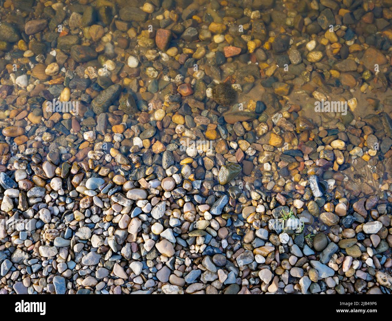 Pebbles at a natural river shore from above. Top down view on small stones with dirt and water ...