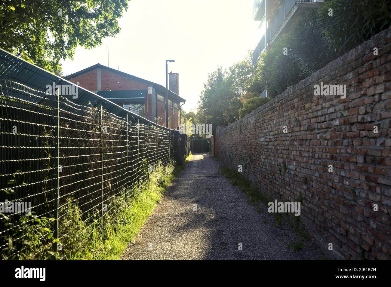 Alley bordered by a fence and a brick wall at sunset Stock Photo - Alamy