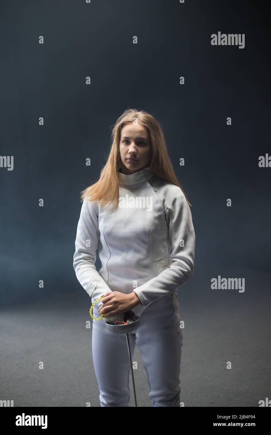 A young woman fencer with her hair down standing with a sword down ...