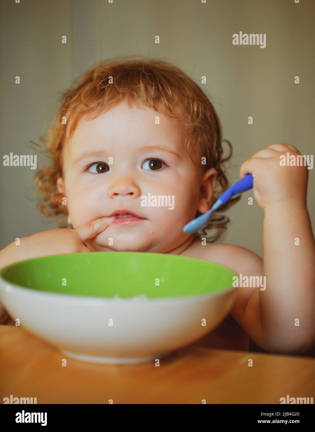Funny baby eating food himself with a spoon on kitchen. Healthy ...