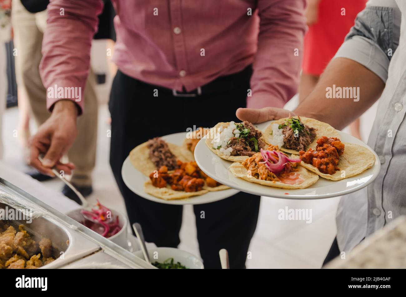 Two men eating tacos at a buffet, they are preparing their food and ...