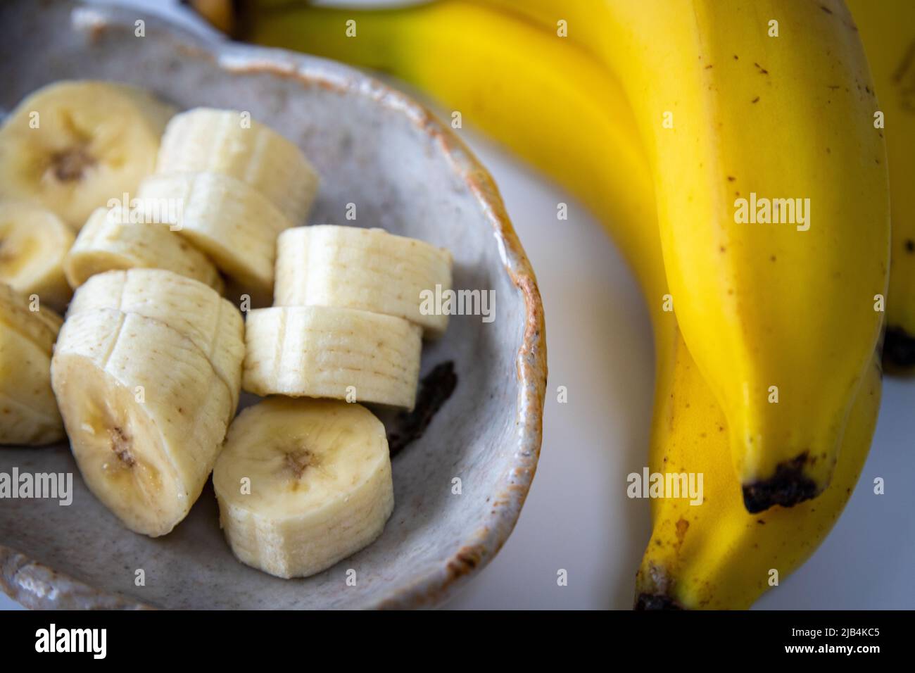 Close up sliced banana on plate and a bunch of bananas on white ...