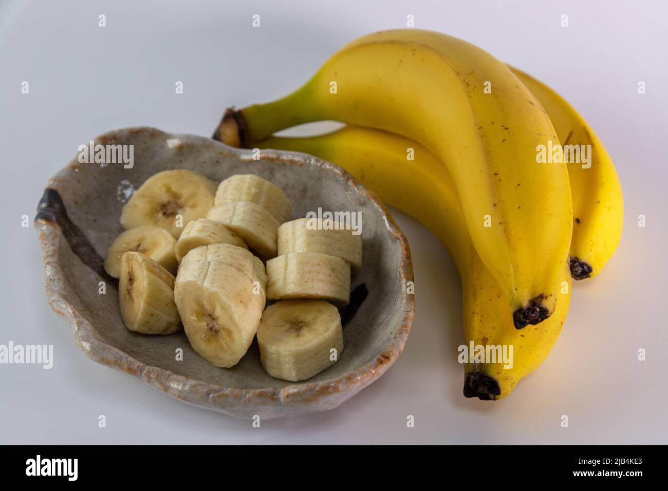 Sliced banana on plate and a bunch of bananas on white background Stock ...