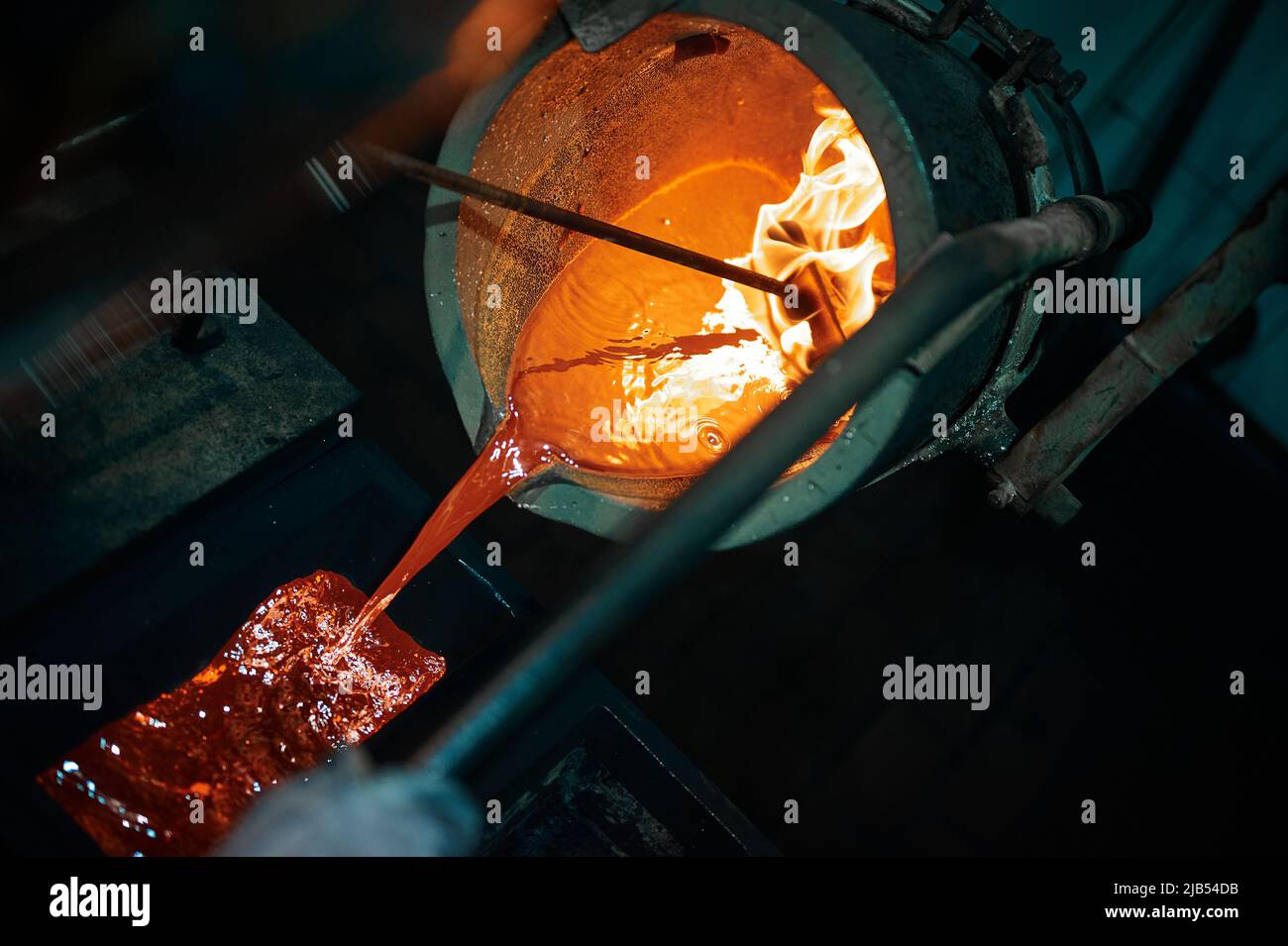 Molten silver is poured from the ladle into a black rectangular ...