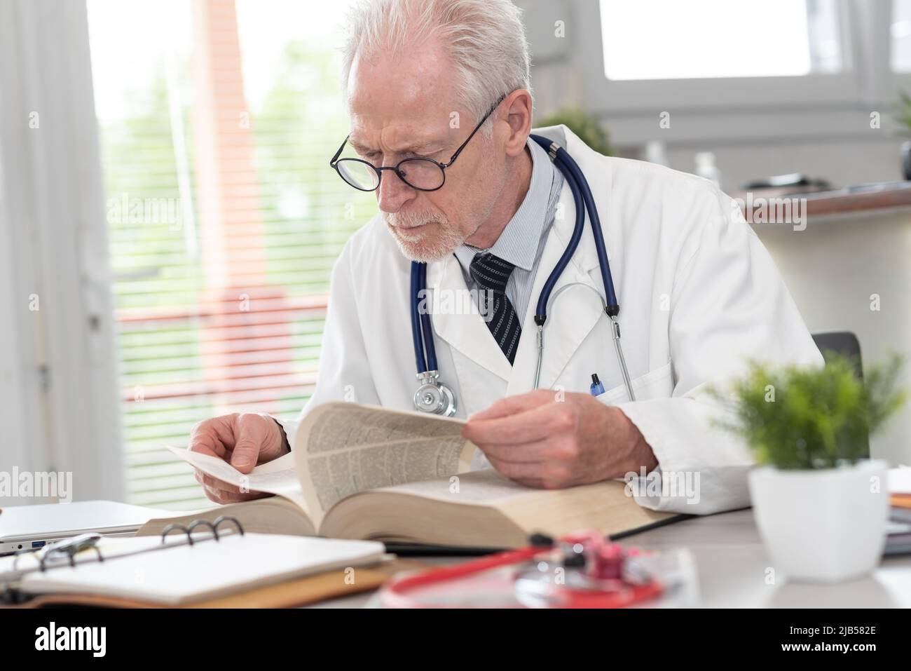 Senior doctor reading a textbook in medical office Stock Photo - Alamy