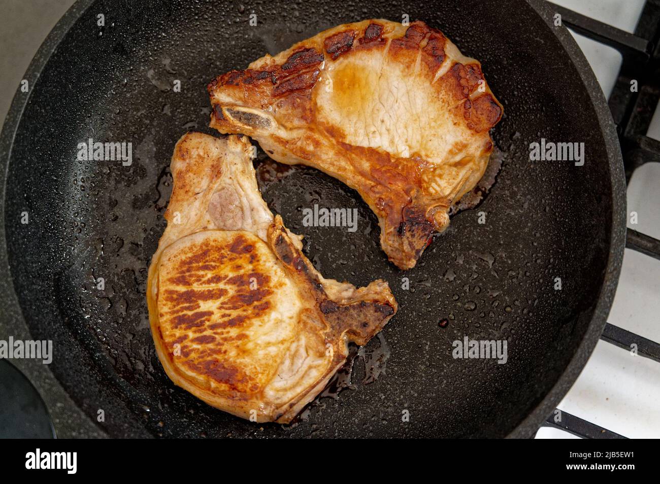 Fried pork steaks with a bone lie in a frying pan. Close-up Stock Photo ...