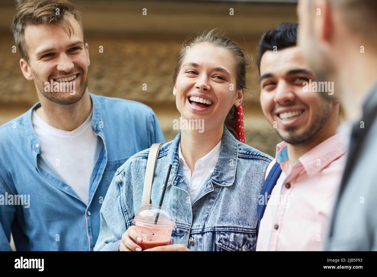 Jolly young people standing outdoors and laughing at joke of friend ...