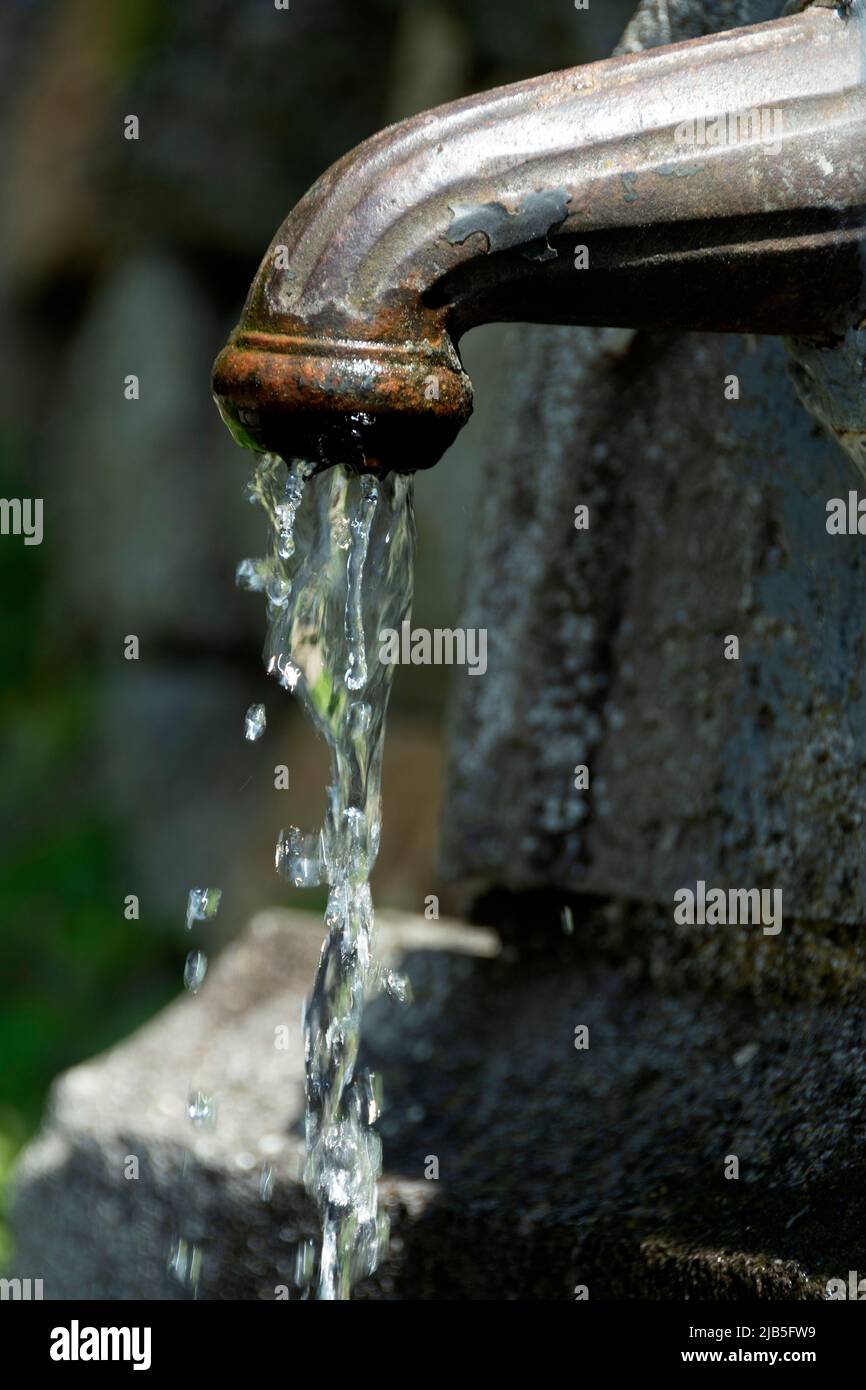 Water flowing from a vintage metal faucet into a stone basin surrounded ...