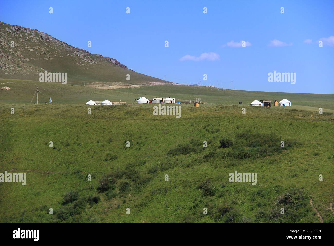 White yurts on a large green hill against the backdrop of a large ...
