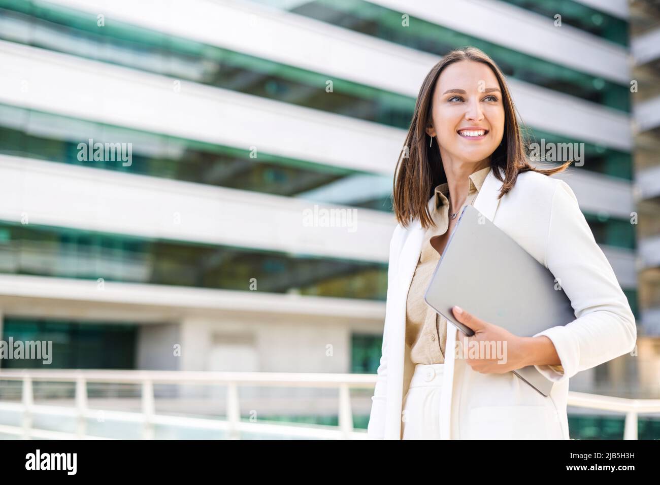 Inspired businesswoman in smart casual wear carrying laptop walking on ...