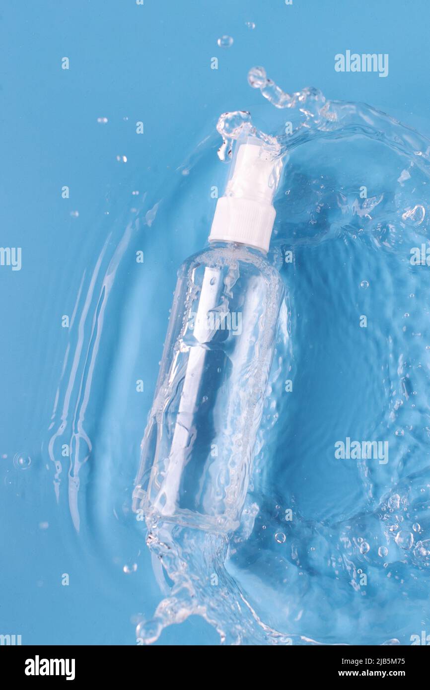 Plastic spray bottle of cosmetic product and splashing water on blue ...