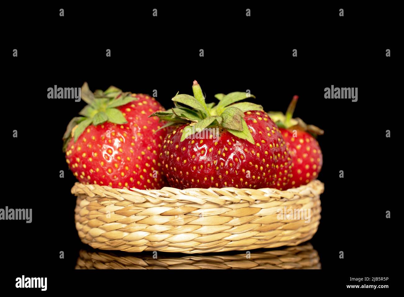 Three berries of ripe organic strawberries on a straw saucer, close-up ...