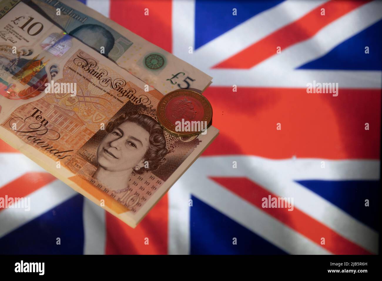 Two British five and ten pound bills and one pound coin on the flag of ...