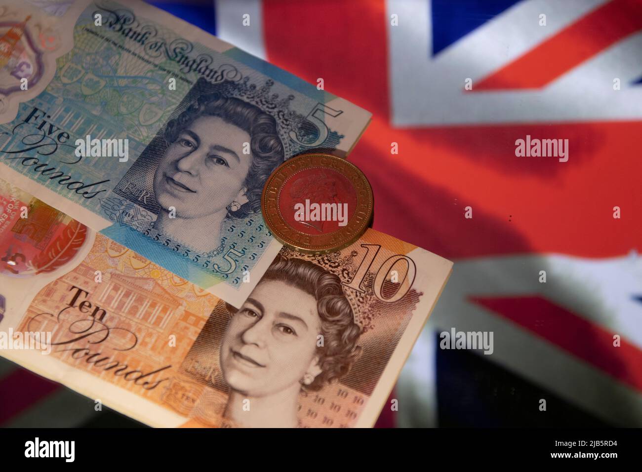 Two British five and ten pound bills and one pound coin on the flag of ...