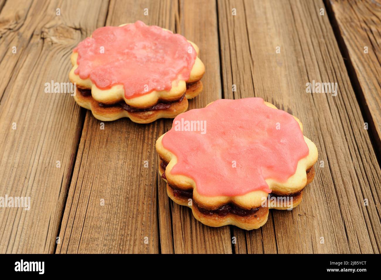 Two double round sand cakes decorated with pink icing and jam on rustic ...