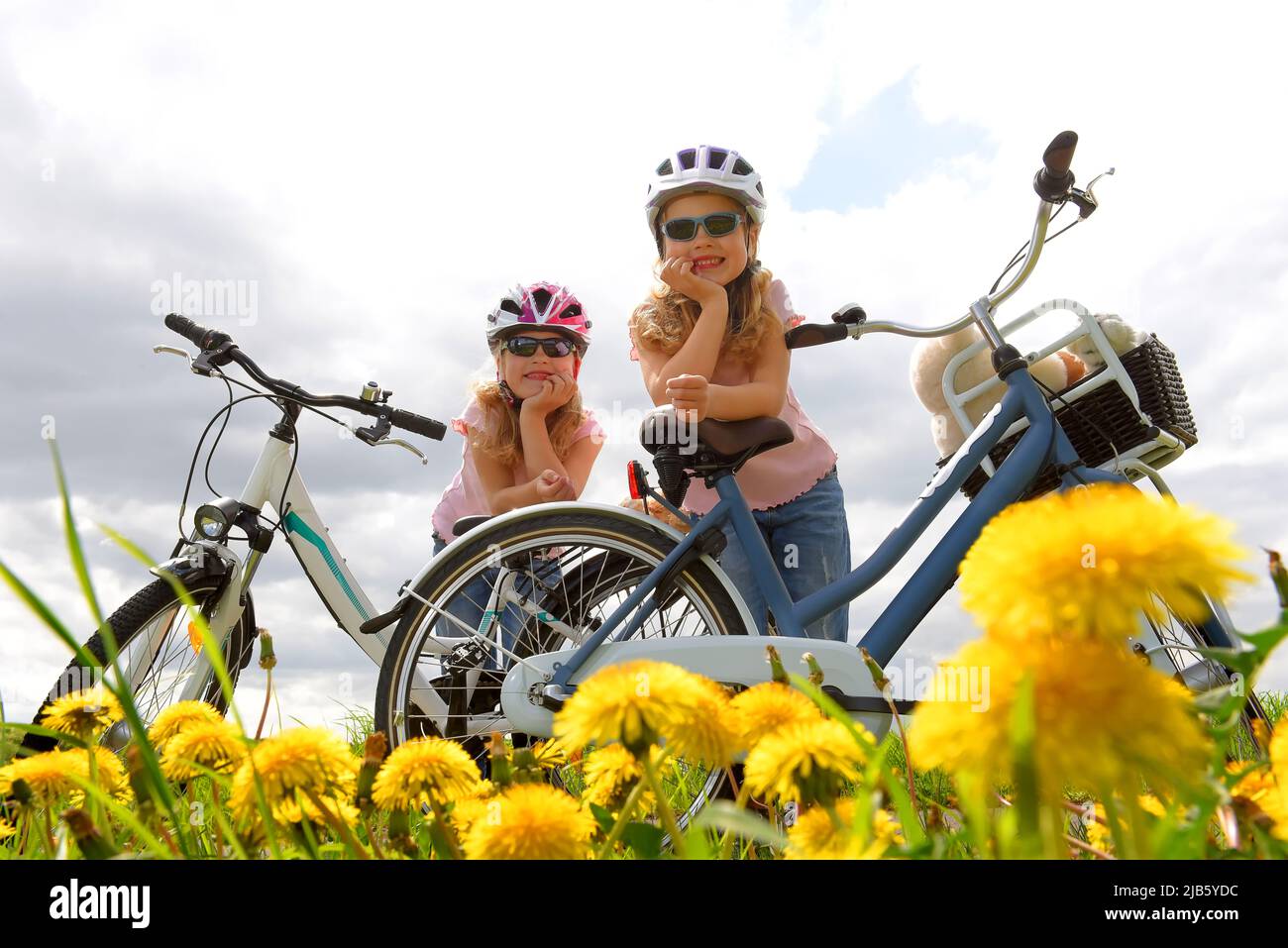 Twin sisters relax from riding their bicycles in front of a dandelion ...