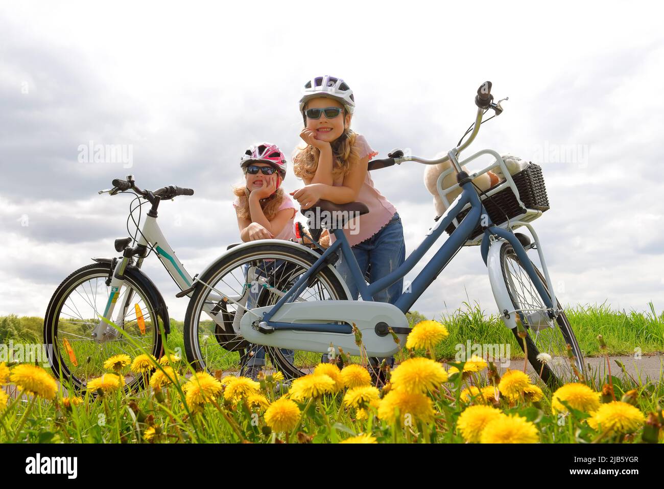Twin sisters relax from riding their bicycles in front of a dandelion ...