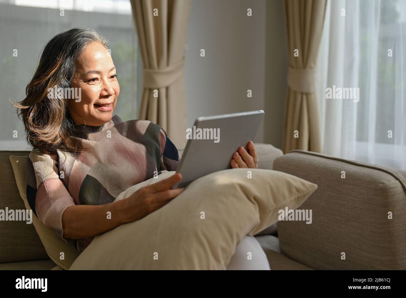 Attractive asian retired woman stay at home, relaxes in the living room ...