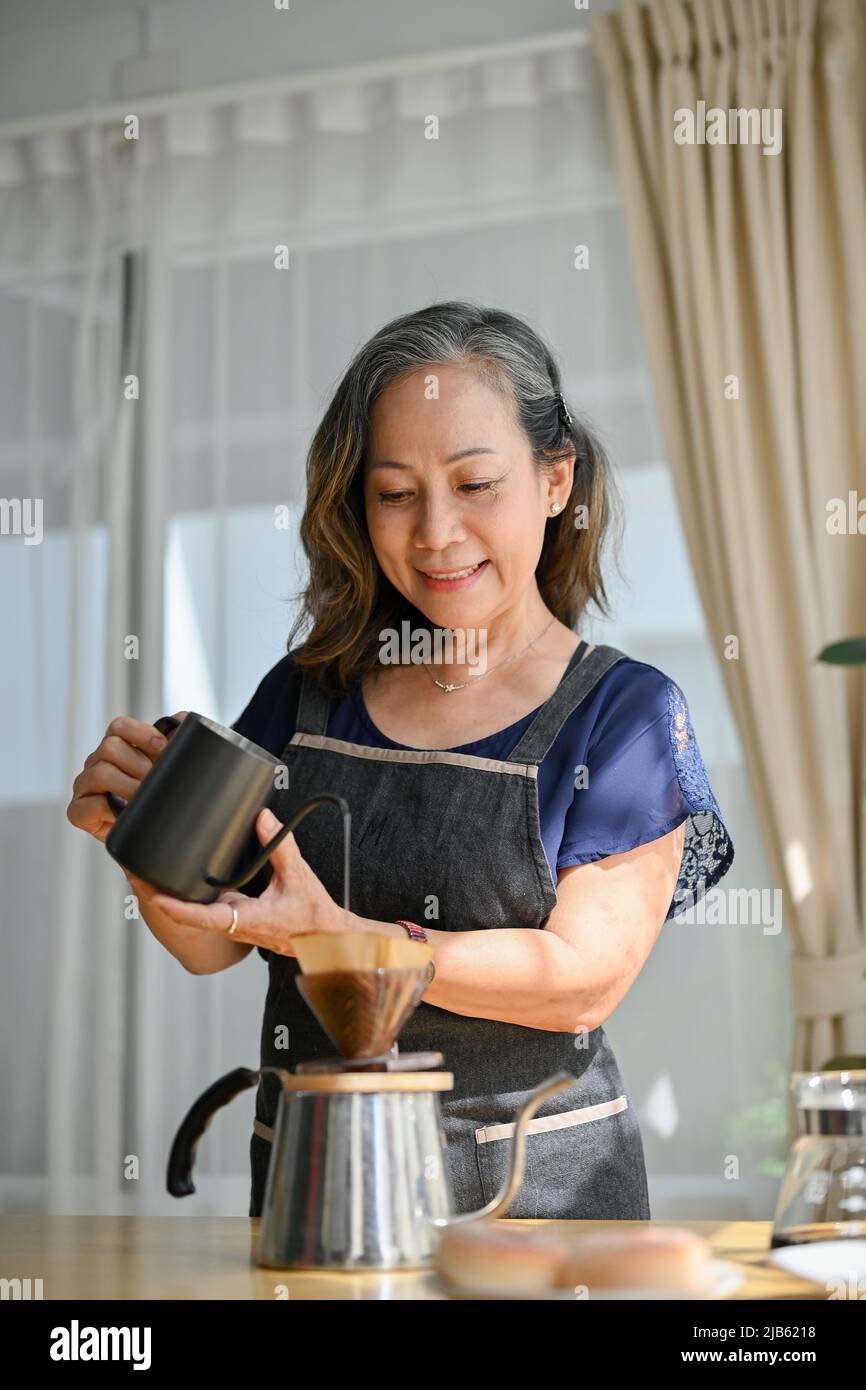 Beautiful Asian retired woman pouring a hot water into a drip coffee ...