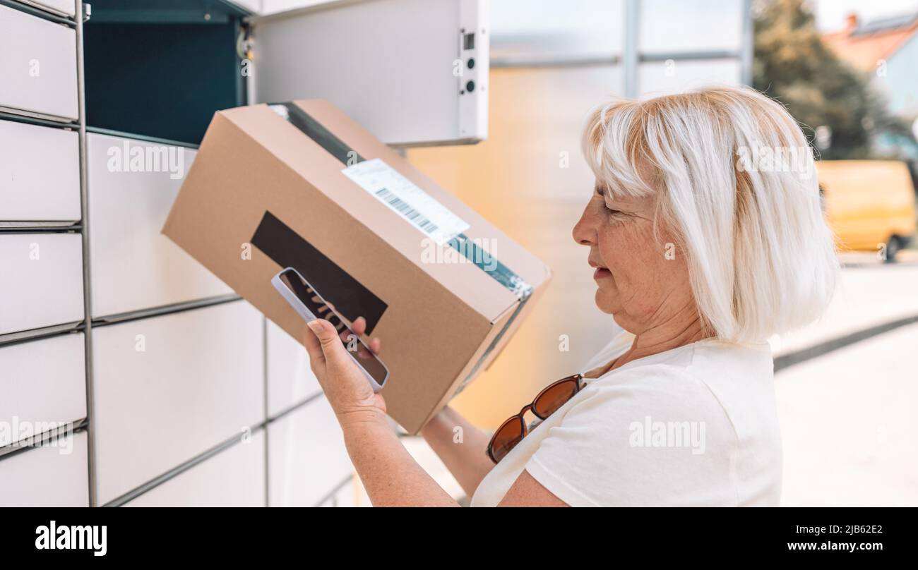 50s caucasian woman getting parcel from cell of automatic post terminal ...
