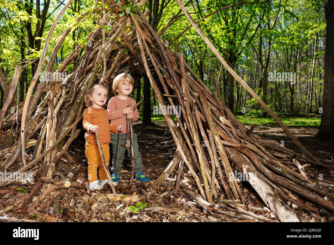 Boy and a girl with wood pile play in hut of branches Stock Photo - Alamy