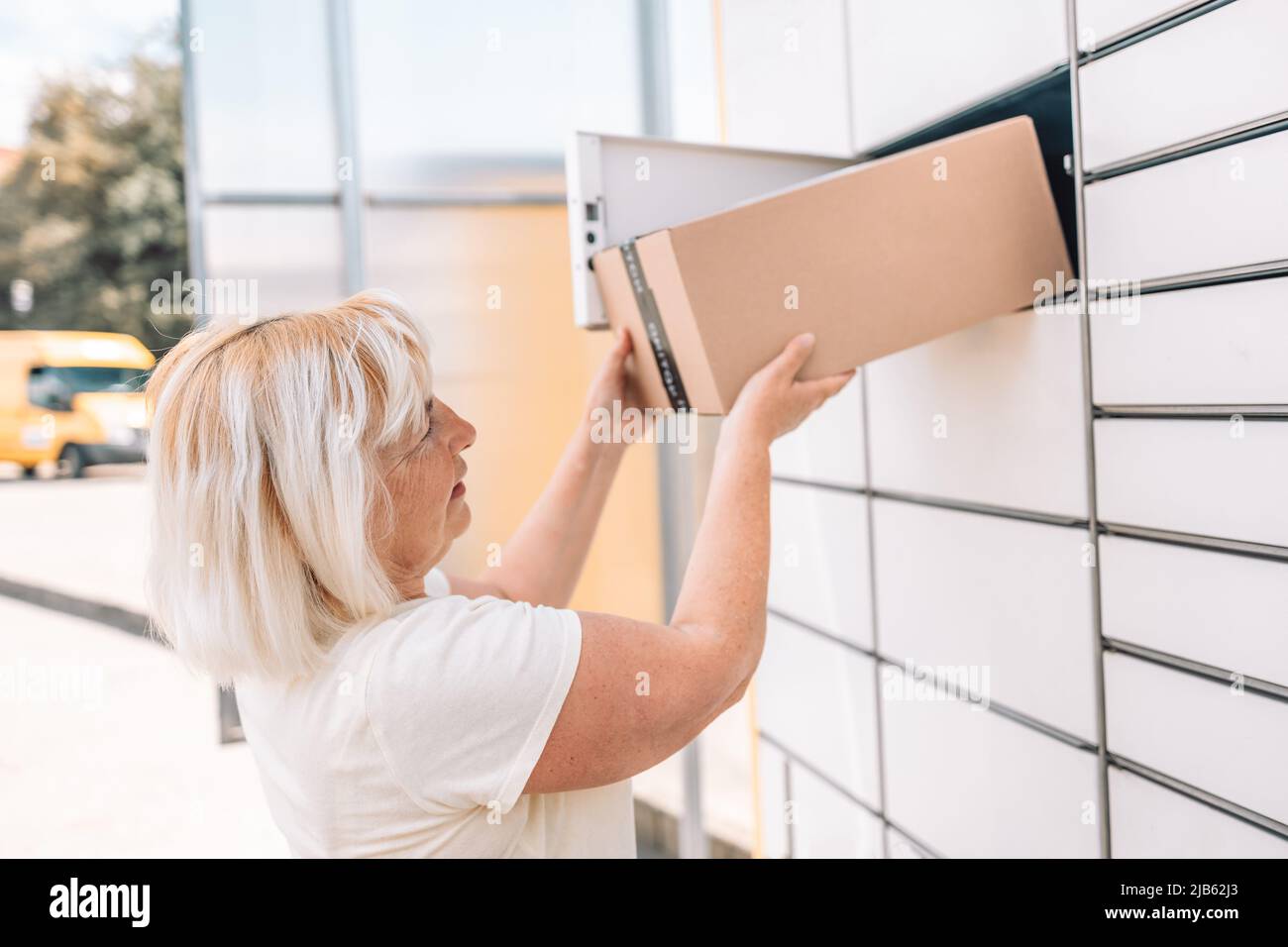 50s caucasian woman getting parcel from cell of automatic post terminal ...