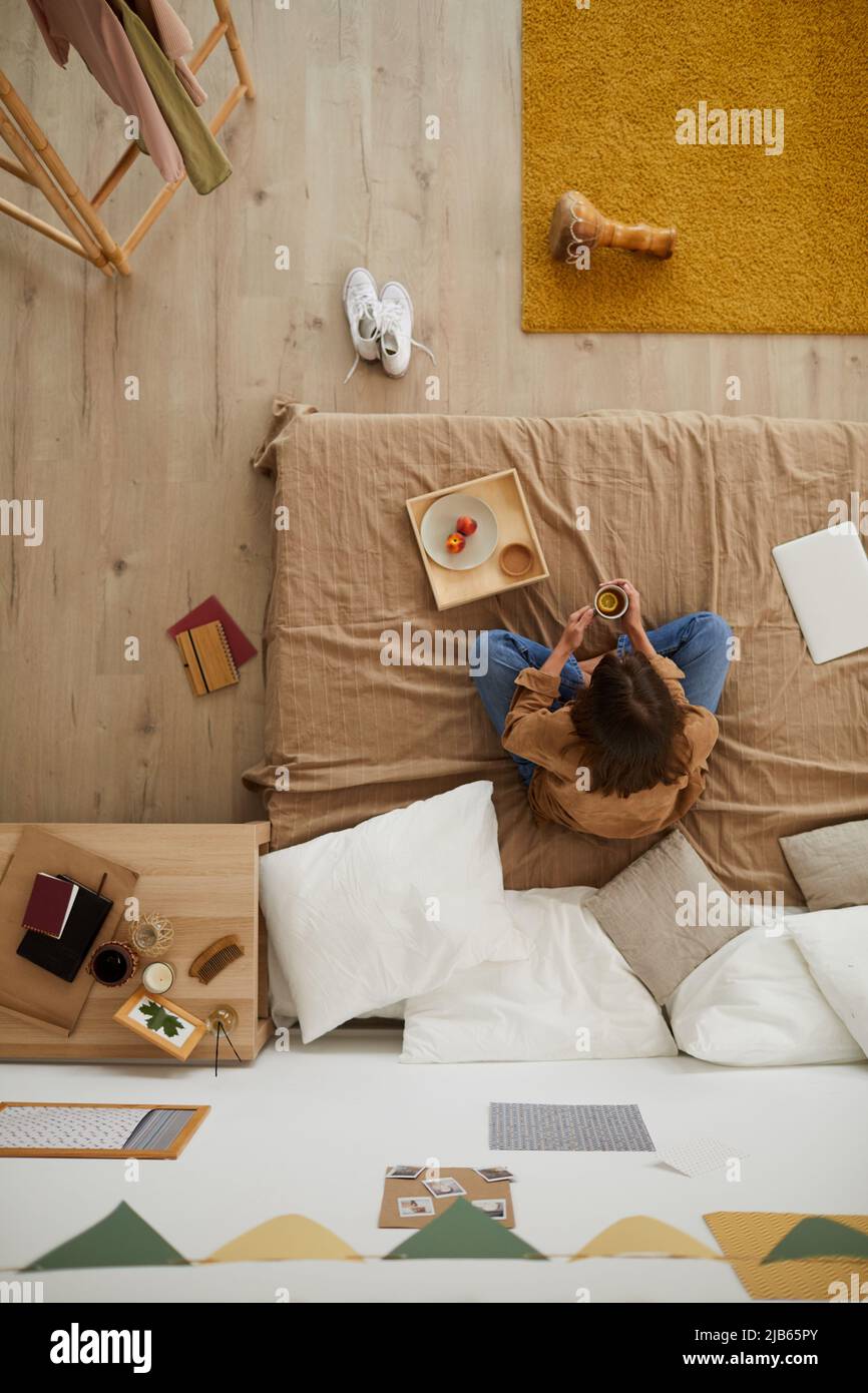High angle view of brunette lady sitting with crossed legs on bed and ...