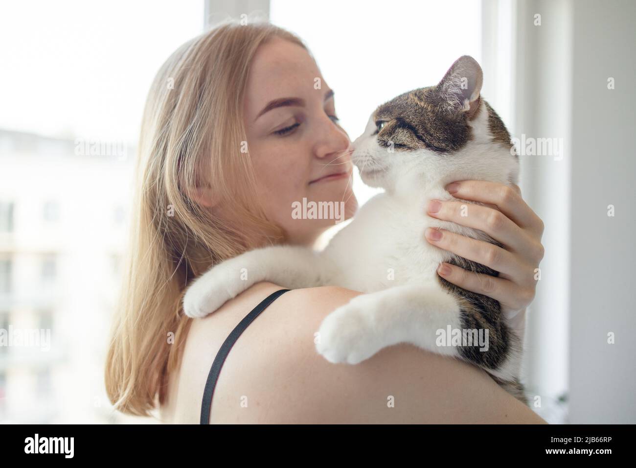 Portrait of young blonde 30s woman holding cute tabby cat with green eyes. Female hugging cat in ...