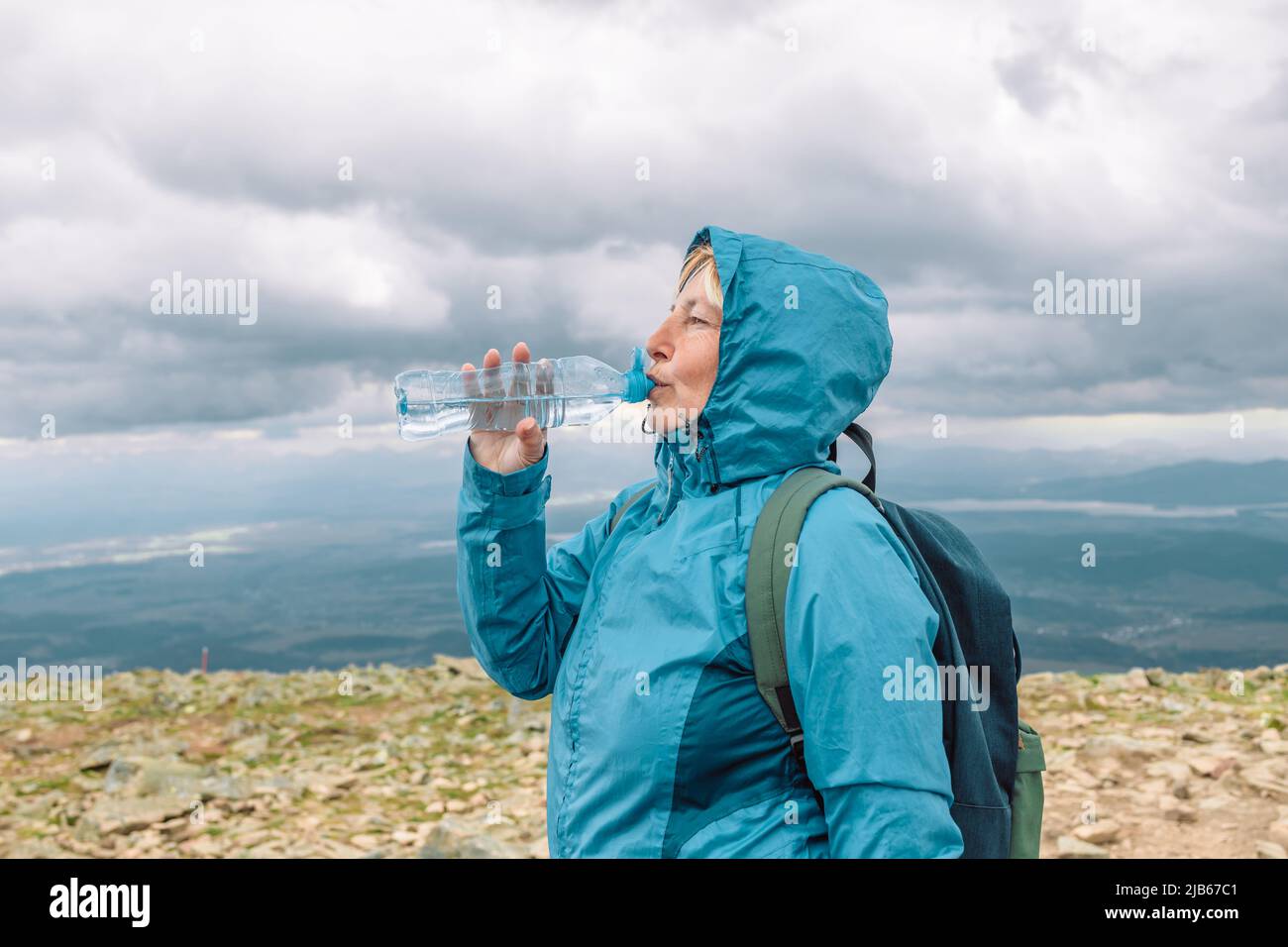 Tired female 50s hiker drinking water from the bottle with backpack ...