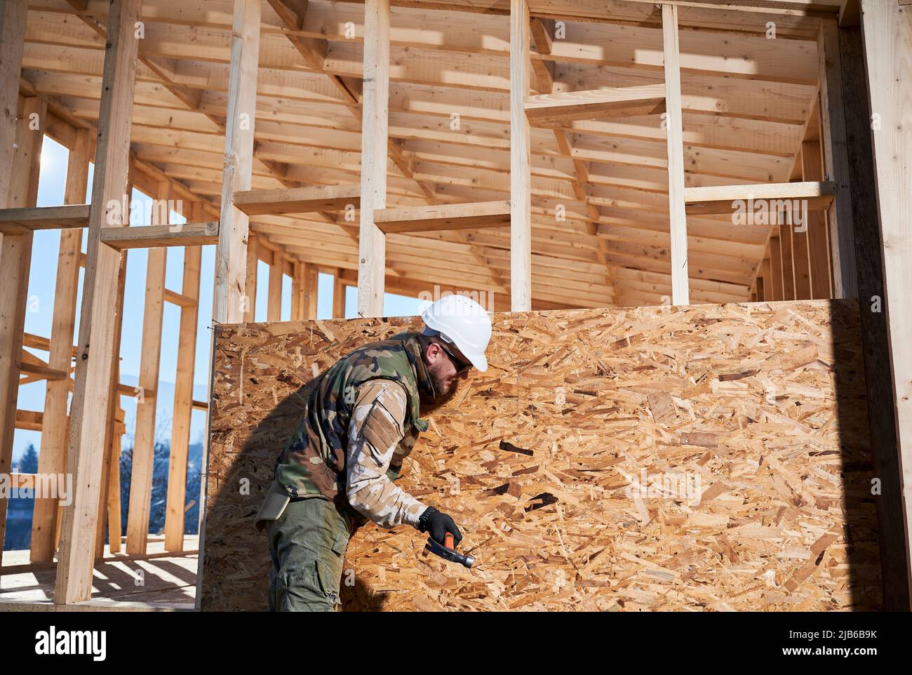 Carpenter hammering nail into OSB panel on the wall of future cottage ...