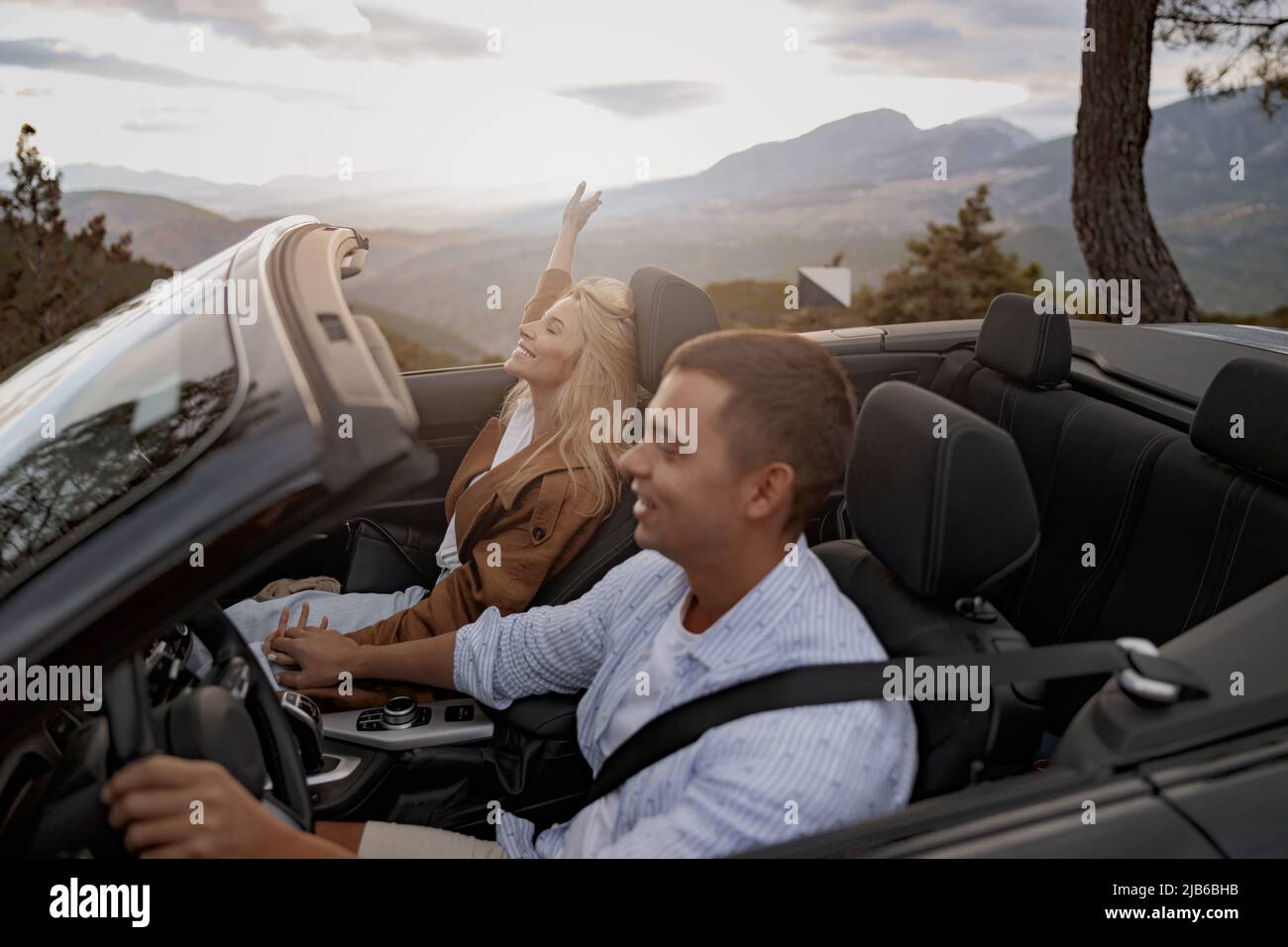 Happy young couple in love driving roofless convertible car holding ...