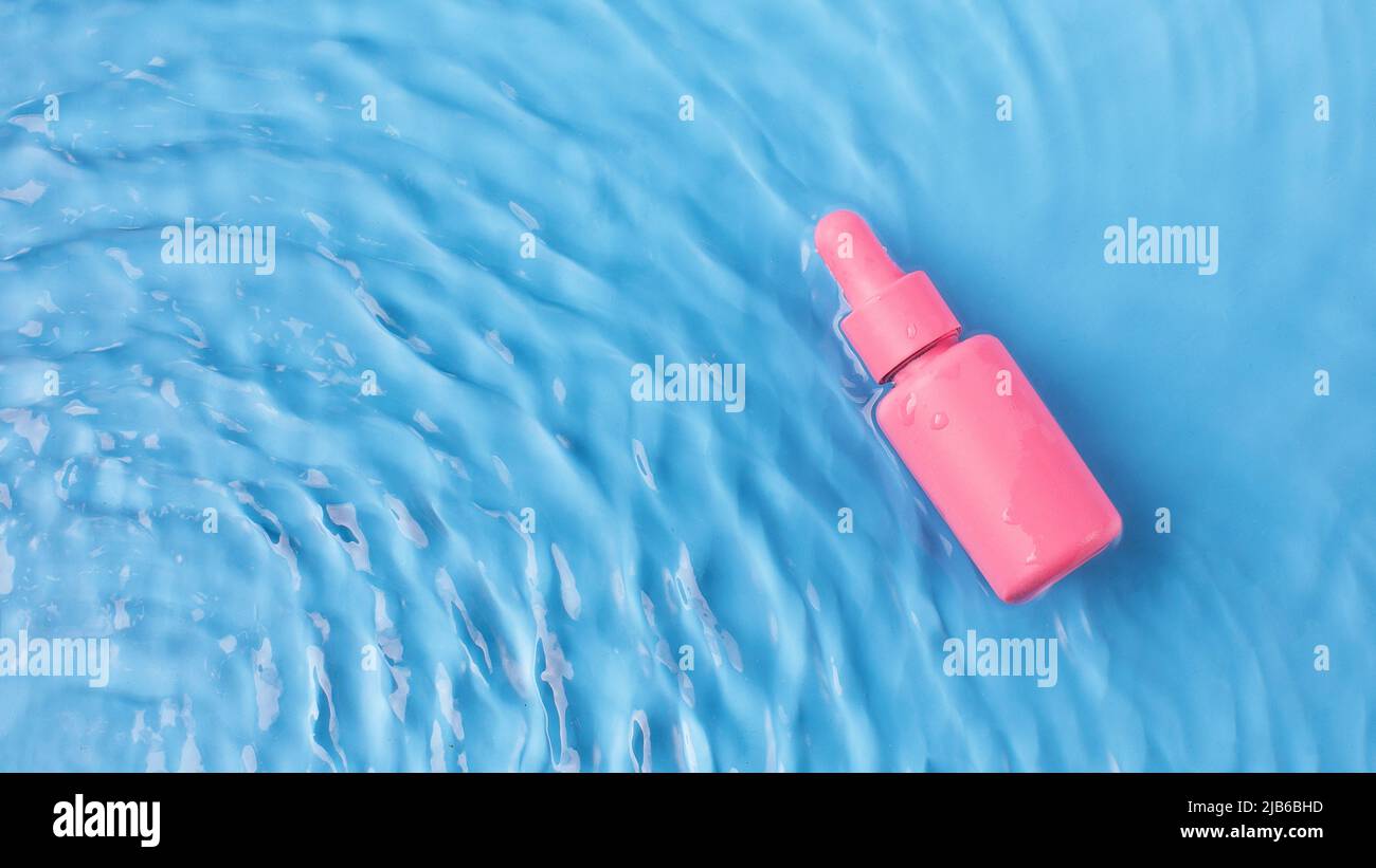 Mock up pink bottle of skincare product and splashing water on blue ...