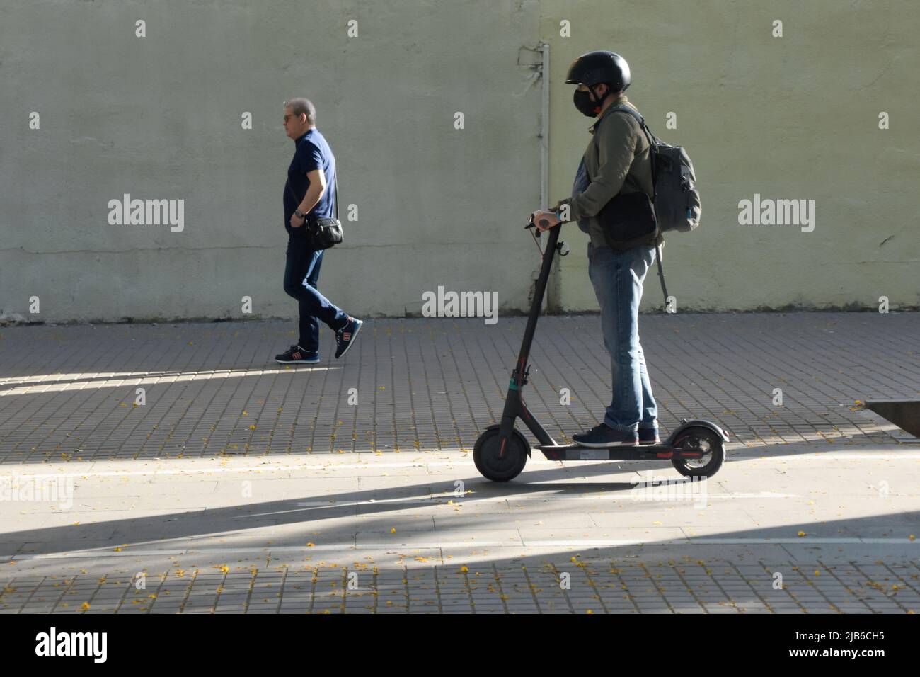 Man with helmet and backpack is riding an electric scooter in a street ...