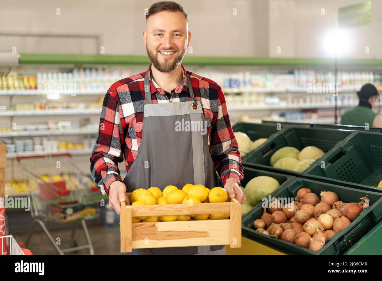 Smiling caucasian worker in a supermarket with lemons looking at camera ...