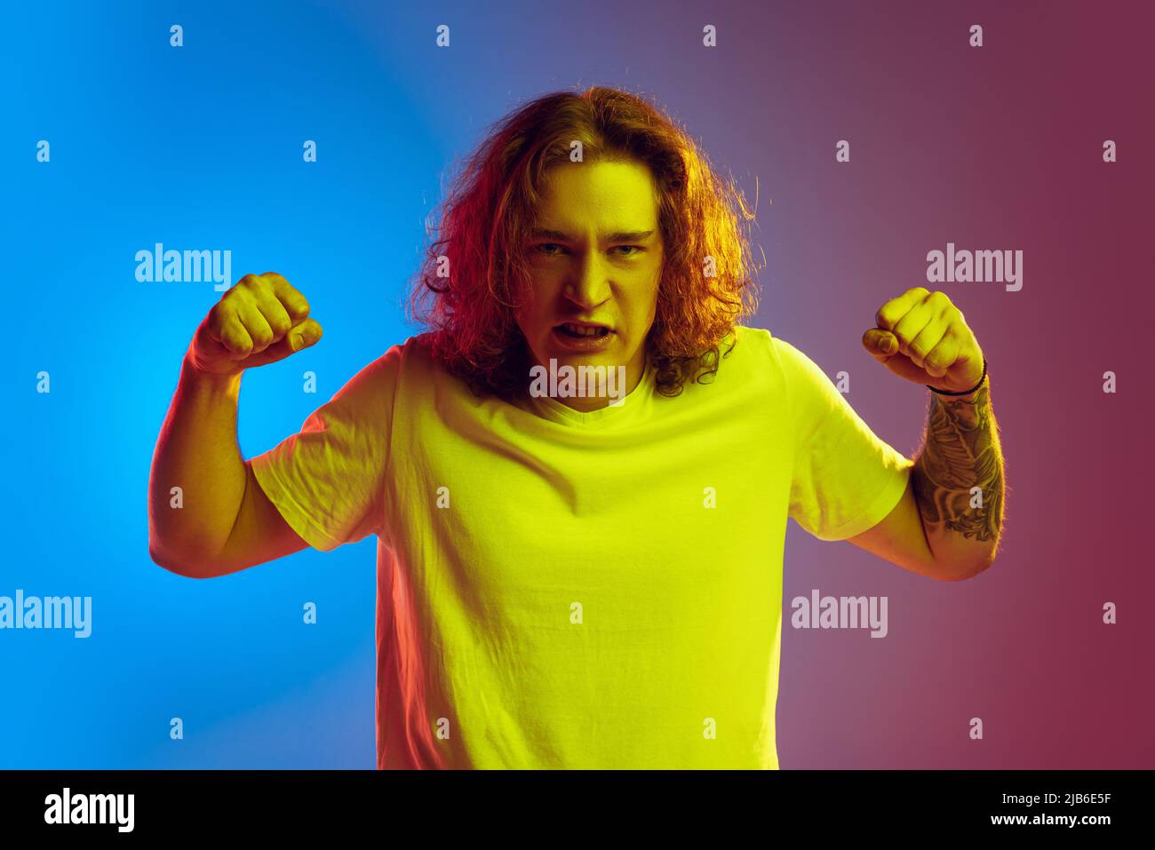Young angry man with long curly hair posing isolated on gradient blue ...