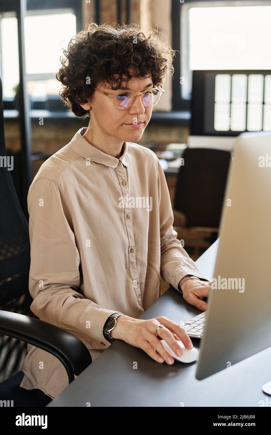 Office employee in eyeglasses sitting at her workplace at office and ...