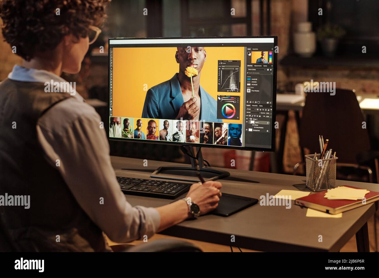 Rear view of designer sitting in front of big monitor and editing ...