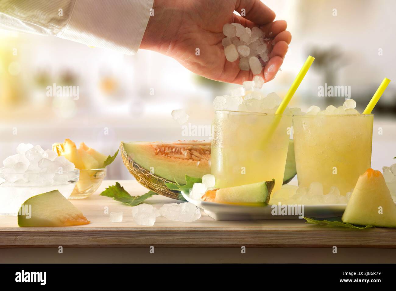 Man preparing refreshing melon drink, throwing cubes into a glass with ...