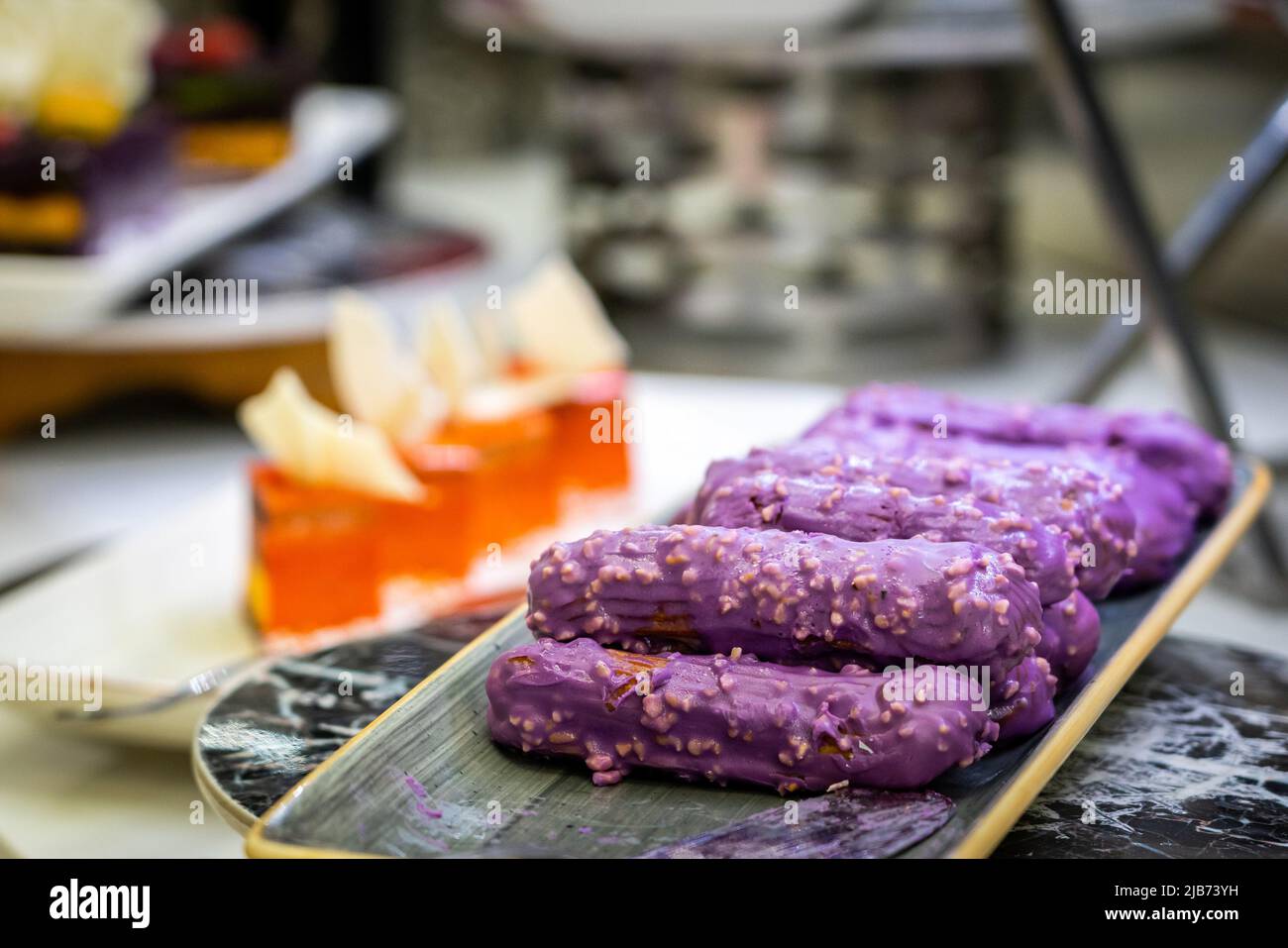 Eclairs with sweet purple topping with nuts on serving plate Stock ...