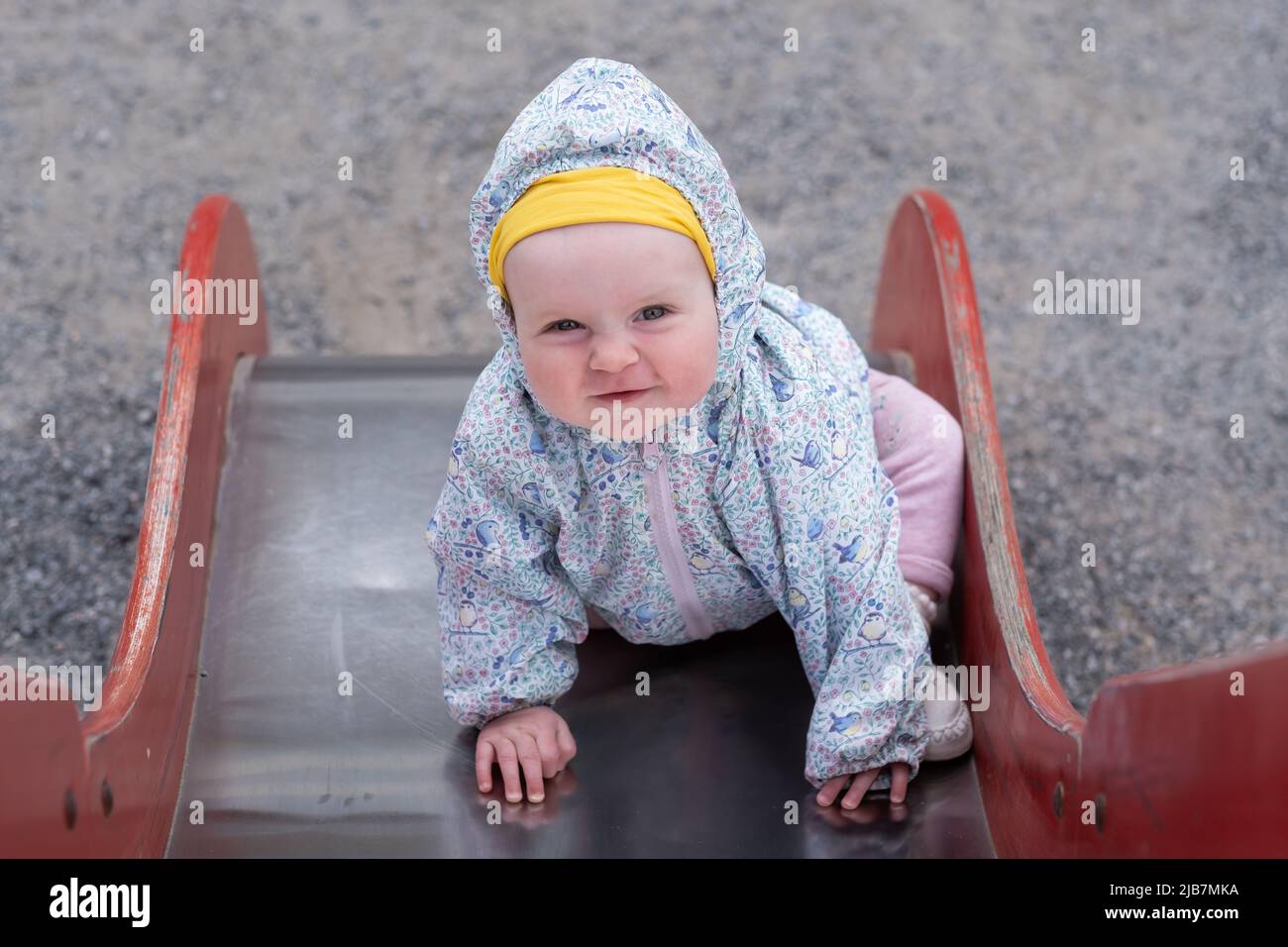 Caucasian baby girl climbing up the slide laughing looking up Stock ...