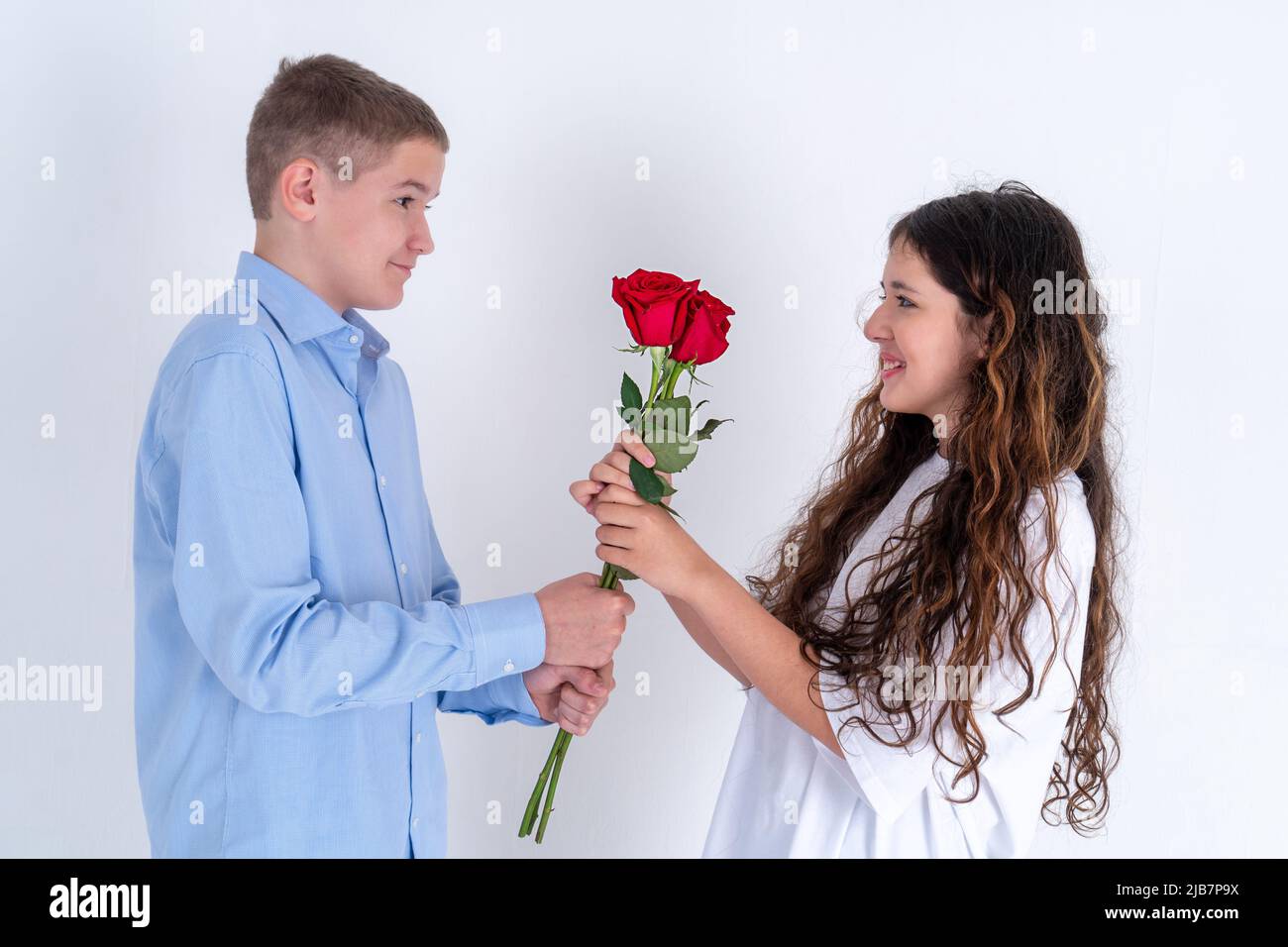 Teen boy gives his girlfriend a bouquet of red roses on a white ...