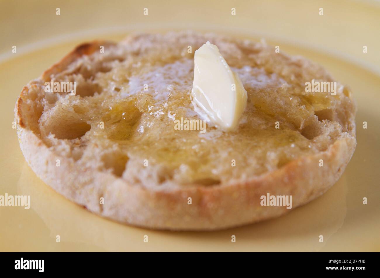 Toasted English muffin with a pat of melting butter on a yellow plate ...