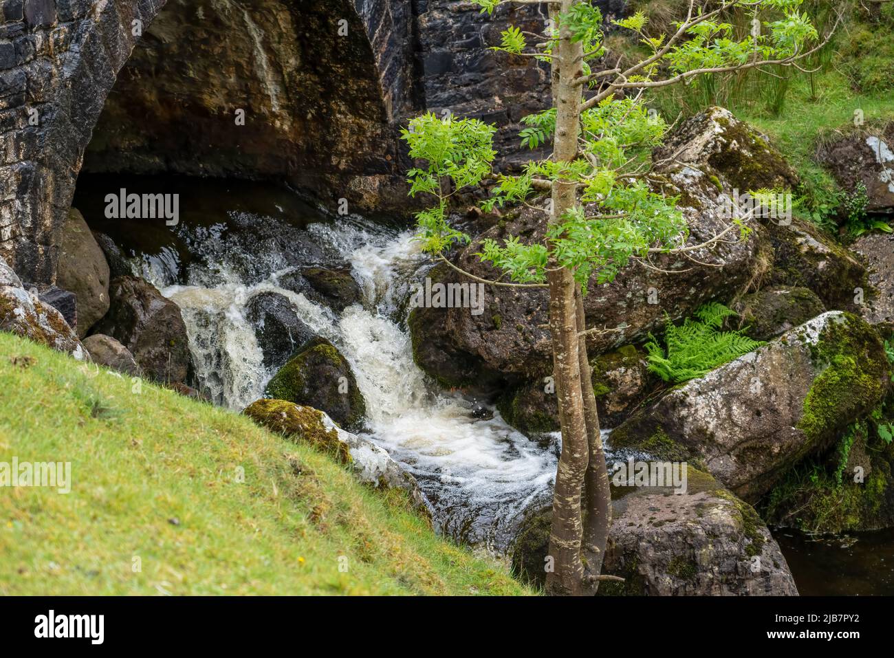 an old stone bridge with boulders beneath the arch on the river bed ...