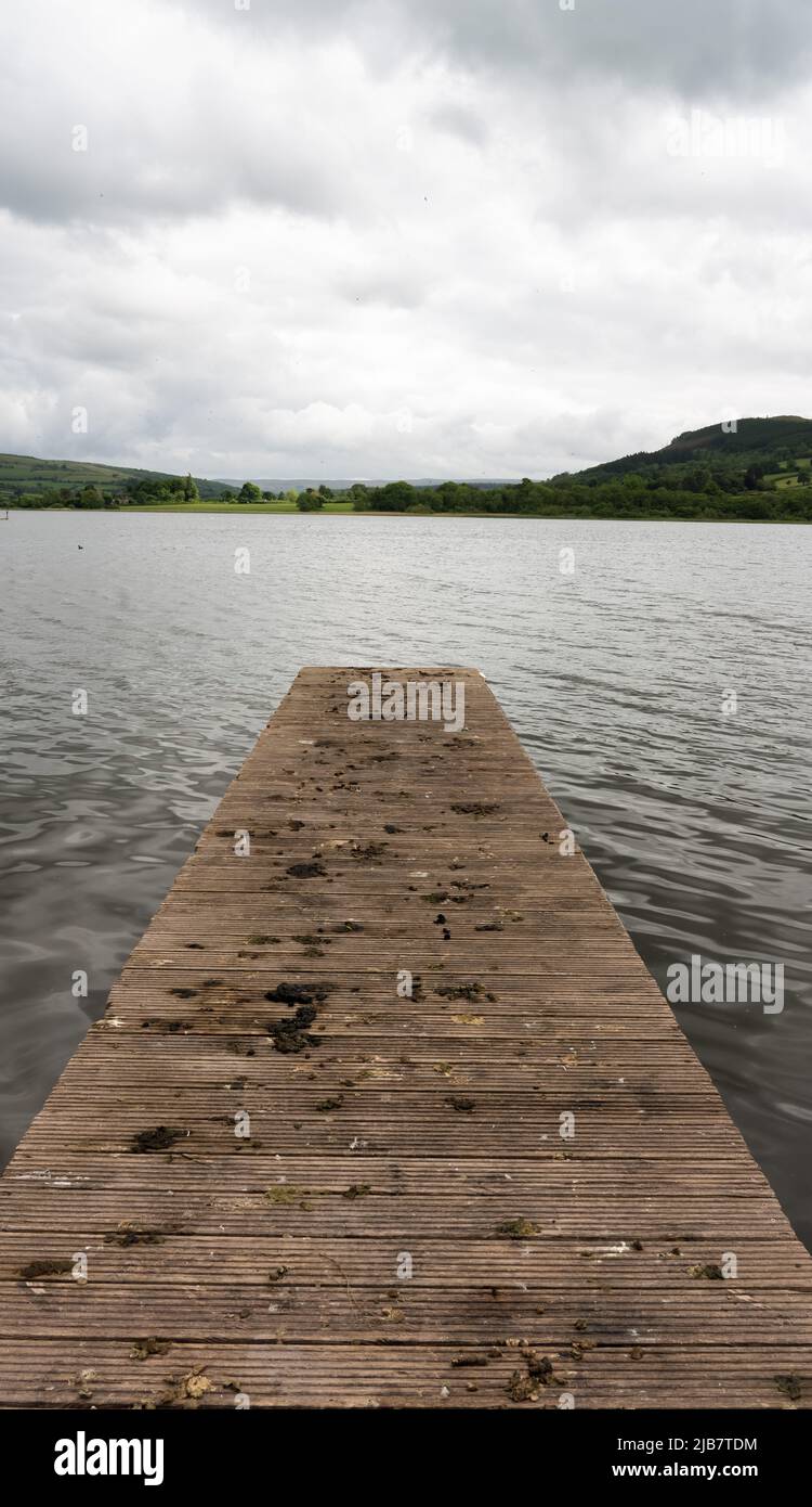 a wooden jetty juts out over a lake with bright white and grey cloud ...
