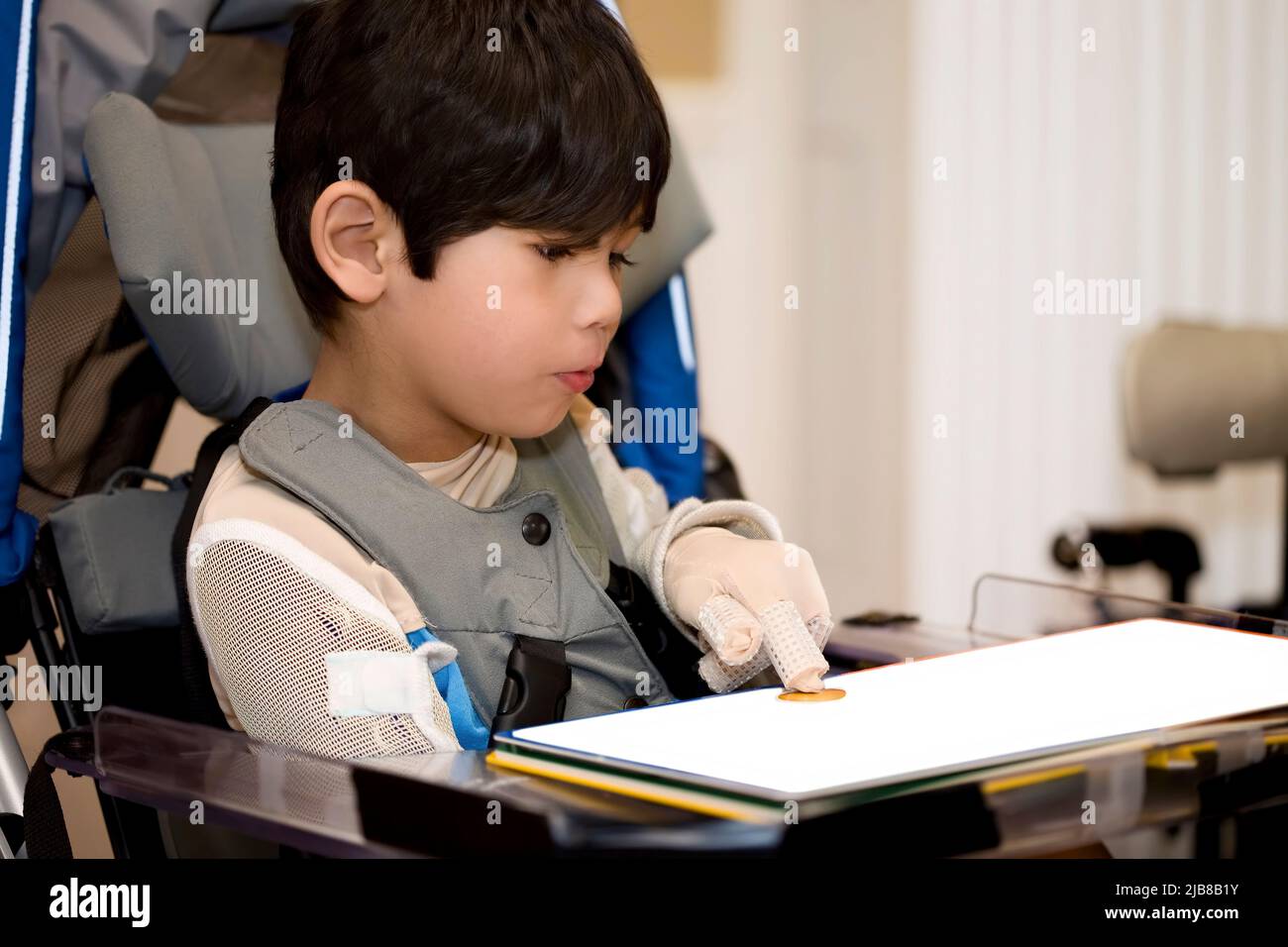 Little boy with disability pointing at book studying in wheelchair at ...